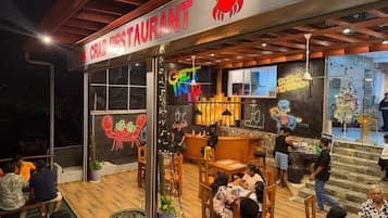 Restaurante com logotipo de caranguejo, mesas ao ar livre e letreiro neon.