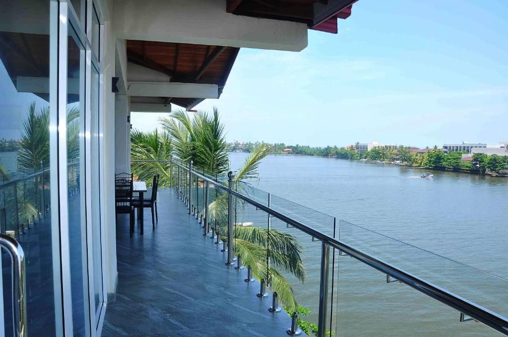 Uma varanda com guarda-corpo de vidro, vista para águas tranquilas, palmeiras e edifícios ao longe.