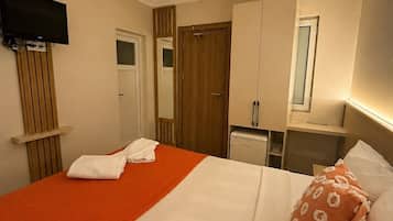 Quarto de hotel com cama, televisão na parede, porta de madeira e uma pequena cozinha.