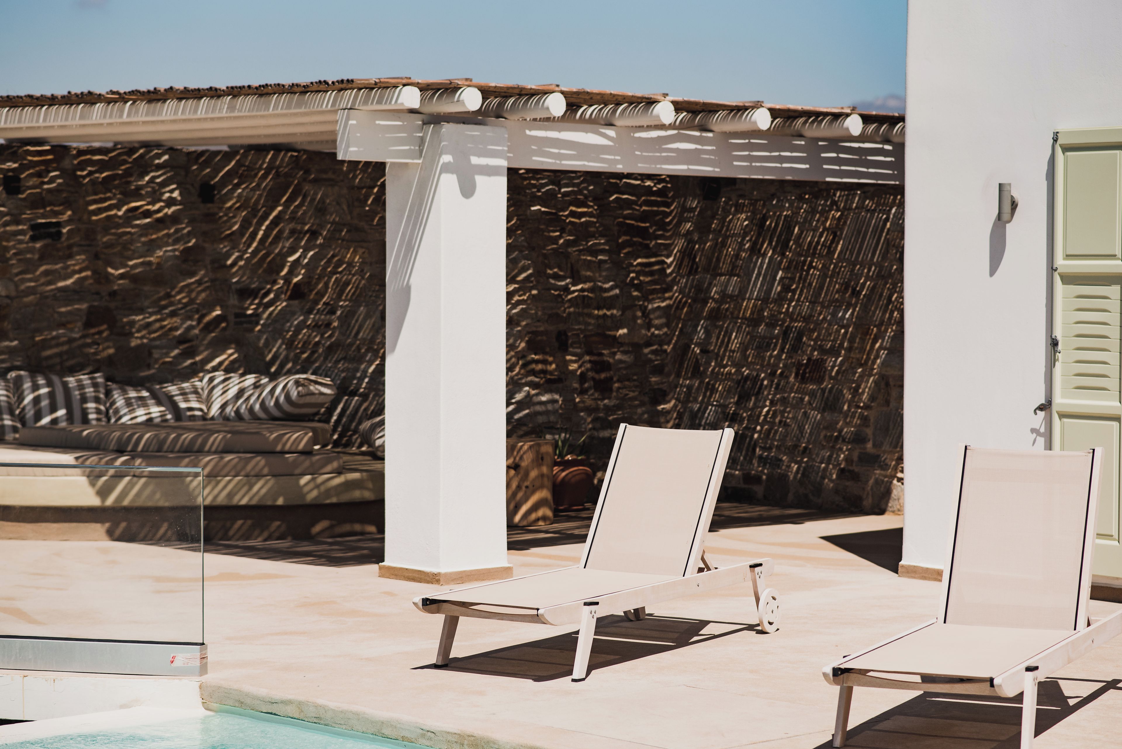 Área de piscina com duas espreguiçadeiras e um muro de pedra ao fundo.