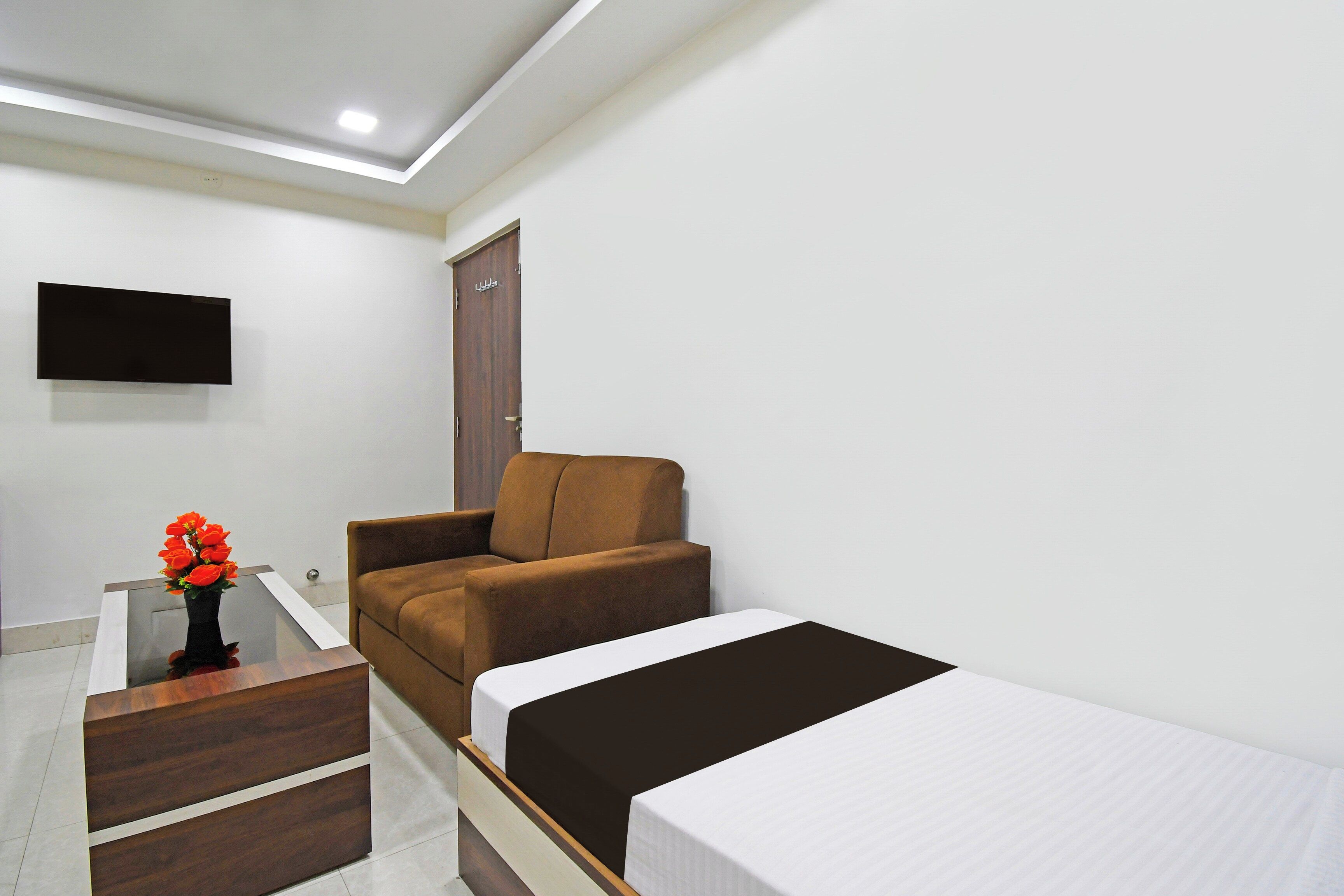 Quarto de hotel com cama, sofá, televisão na parede e uma pequena mesa com um vaso de flores.