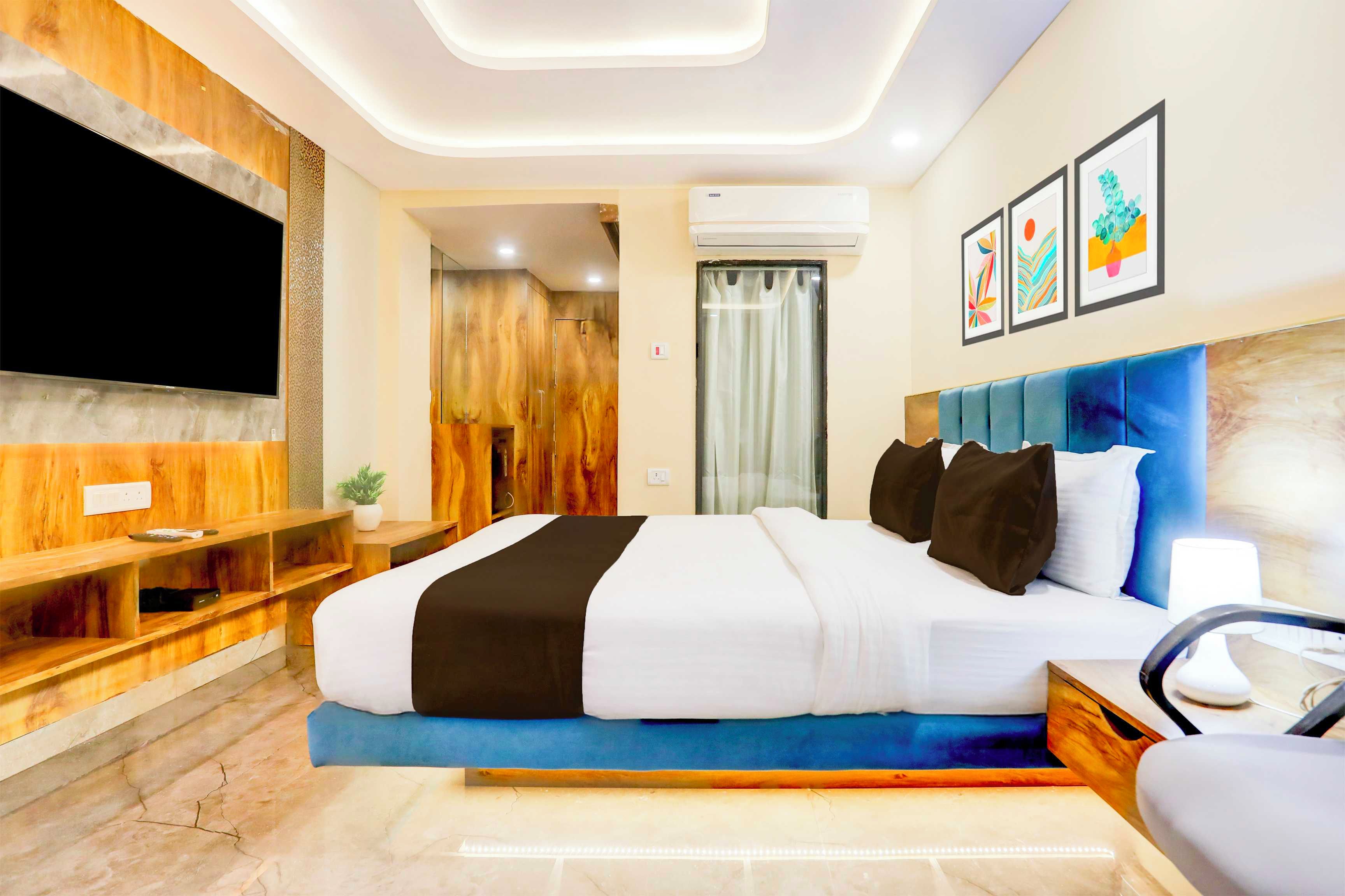 Quarto de hotel moderno com uma cama grande, televisão de tela plana, parede de destaque em madeira e teto com iluminação embutida.