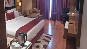 Quarto de hotel com cama, escrivaninha, cadeira, televisão e um quadro na parede.