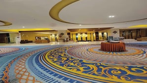 Um hall amplo com um tapete de padrão circular, um balcão de recepção e uma área de estar.