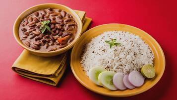 Uma tigela de curry com feijão e um prato de arroz com fatias de pepino e um gomo de limão.