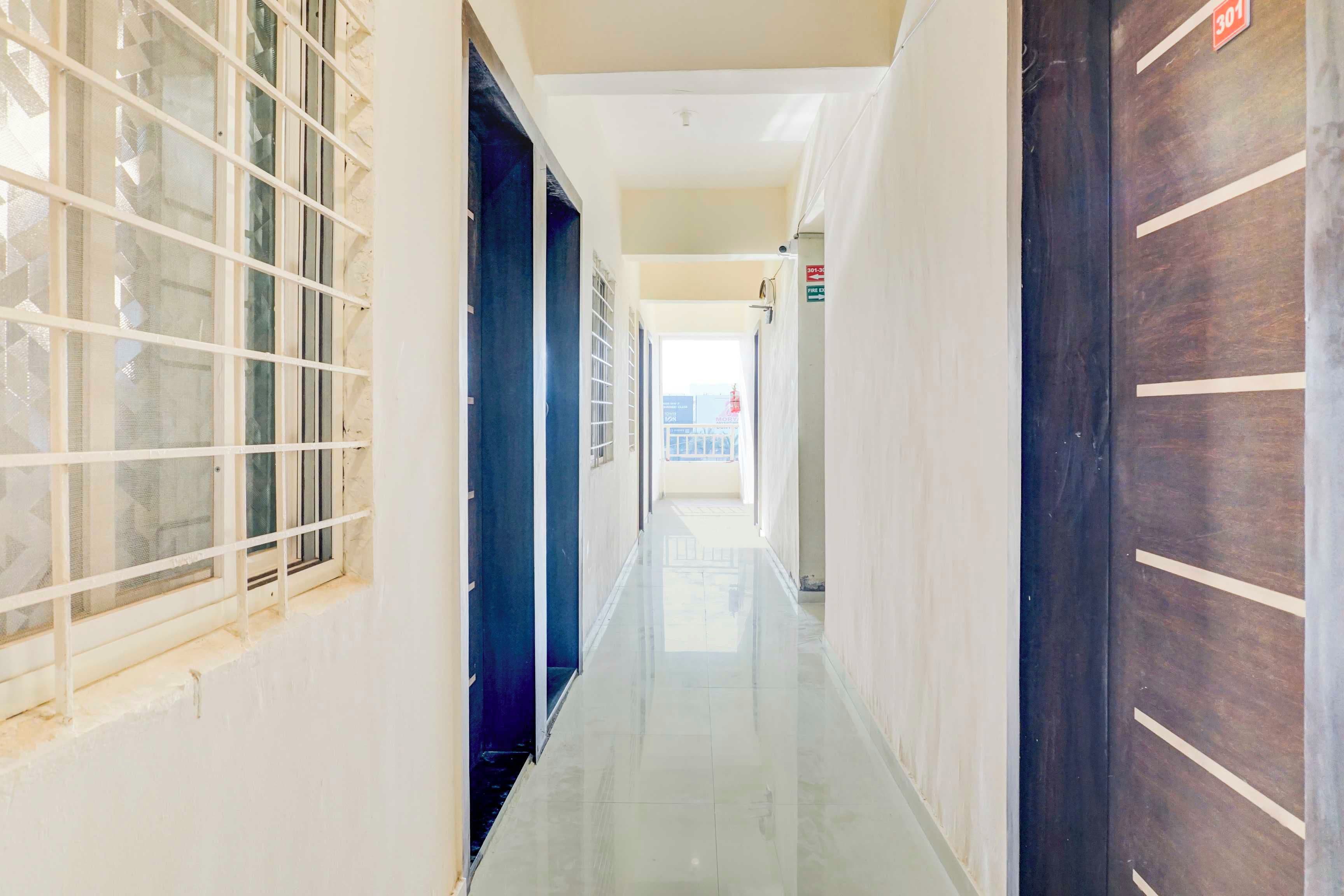 Corredor com sinalização de saída de incêndio, porta com placa de número e janela com grades.