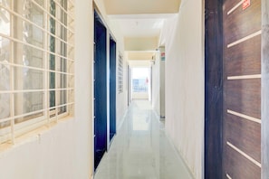 Corredor com sinalização de saída de incêndio, porta com placa de número e janela com grades.
