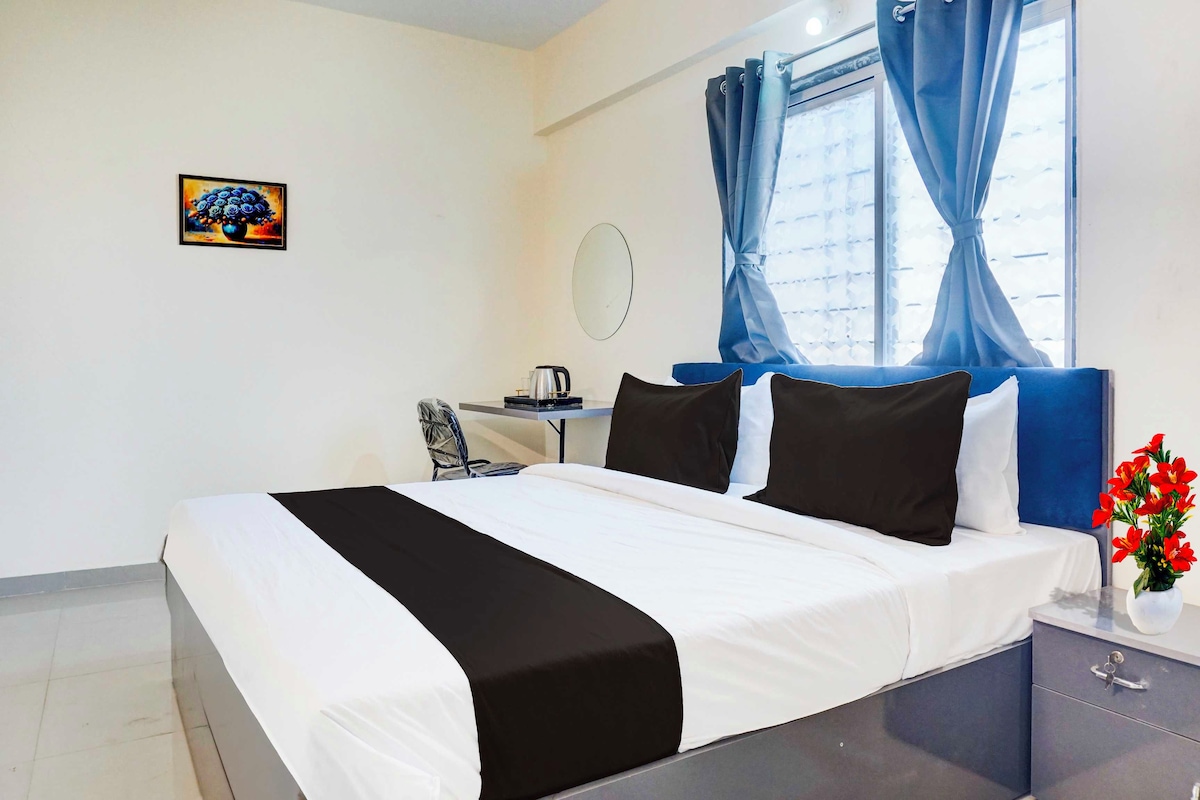 Quarto de hotel com cama, escrivaninha, cadeira, mesa de cabeceira, vaso com flores e um quadro na parede.