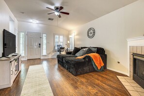 Uma sala de estar ampla com piso de madeira, um sofá preto, lareira e ventilador de teto.