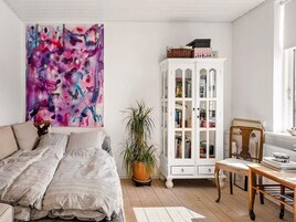 Quarto com cama, armário branco com portas de vidro, pintura abstrata grande e planta em vaso.