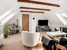 Uma sala de estar estilo loft com vigas de madeira, um sofá branco, uma televisão e estantes.