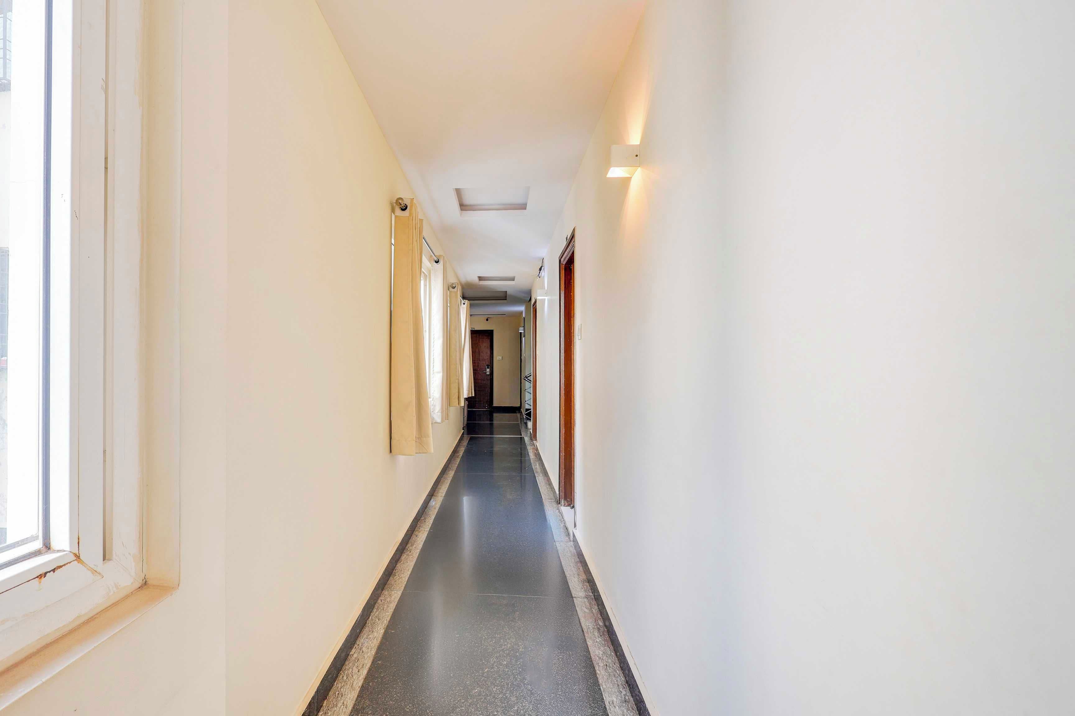 Um corredor comprido e estreito com piso escuro, paredes brancas e teto com iluminação embutida.