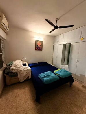 Quarto com cama, ventoinha no teto, guarda-roupa e um quadro na parede.