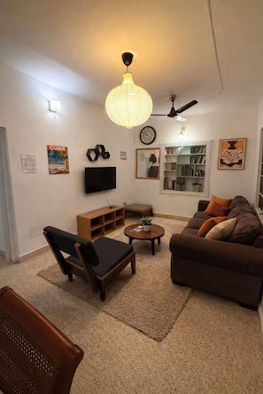 Sala de estar com sofá, poltrona, mesa de centro, estante e televisão na parede.