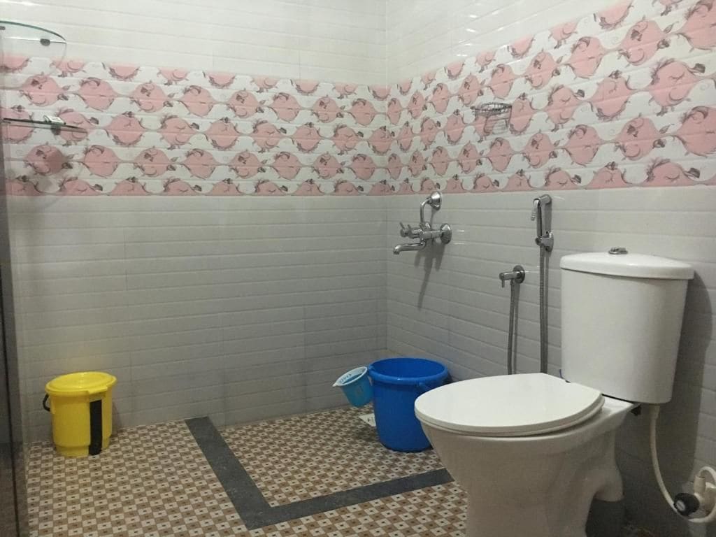 Casa de banho com parede estampada, sanita, chuveiro e dois baldes.