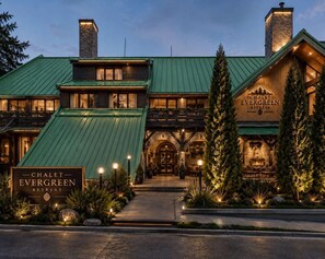 Um edifício em estilo chalé com telhado verde, um letreiro com a inscrição 'Chalet Evergreen Retreat' e um restaurante chamado 'Chalet Evergreen Restaurant'.