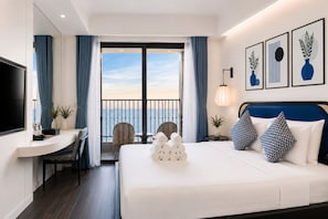 Quarto de hotel com cama, escrivaninha, cadeira, televisão e varanda com vista.