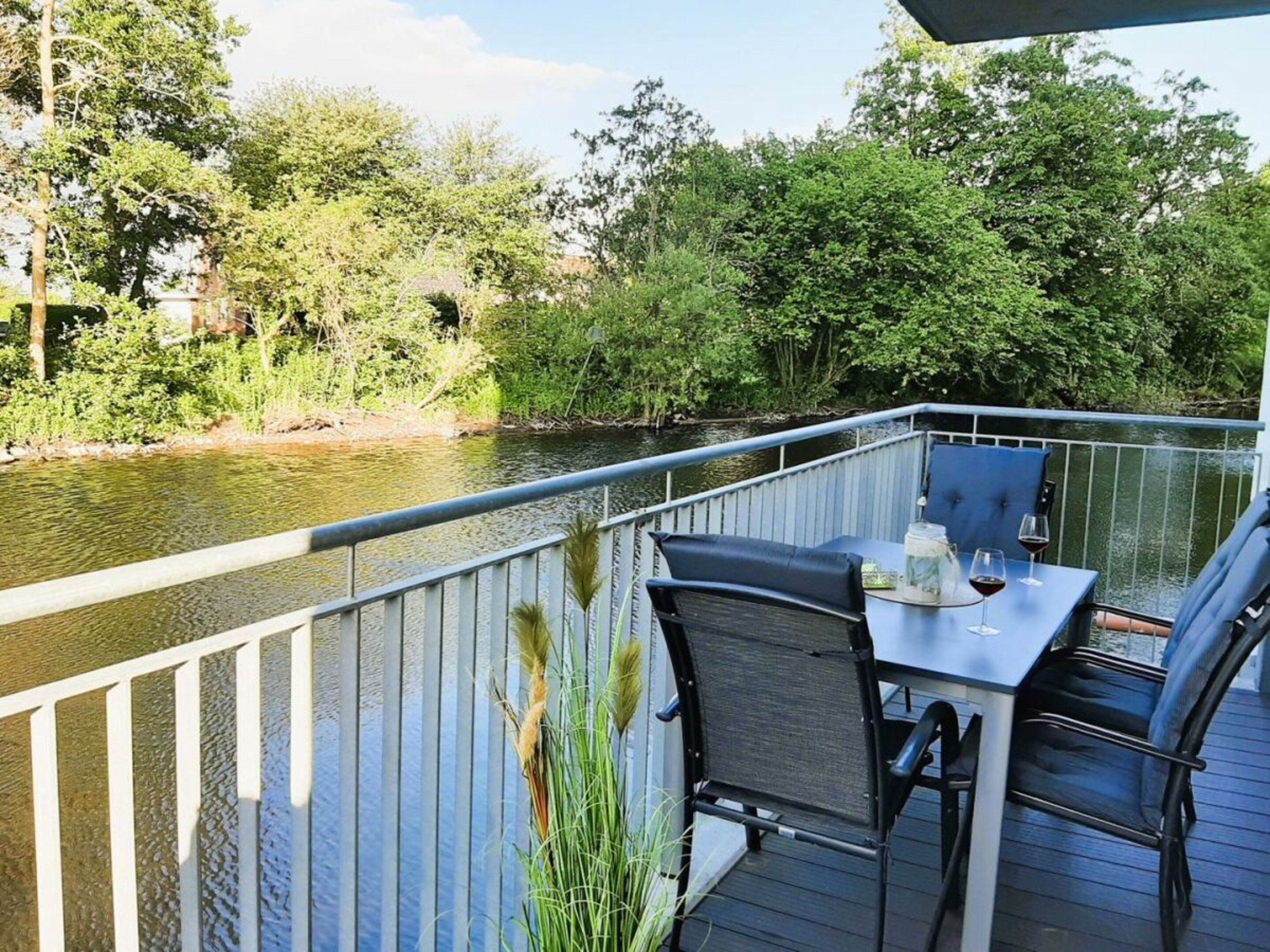 Um terraço com mesa e cadeiras oferece vista para um rio, cercado por vegetação.