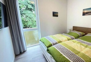 Quarto com uma grande janela, uma cama com roupa de cama listrada e um pequeno quadro na parede.
