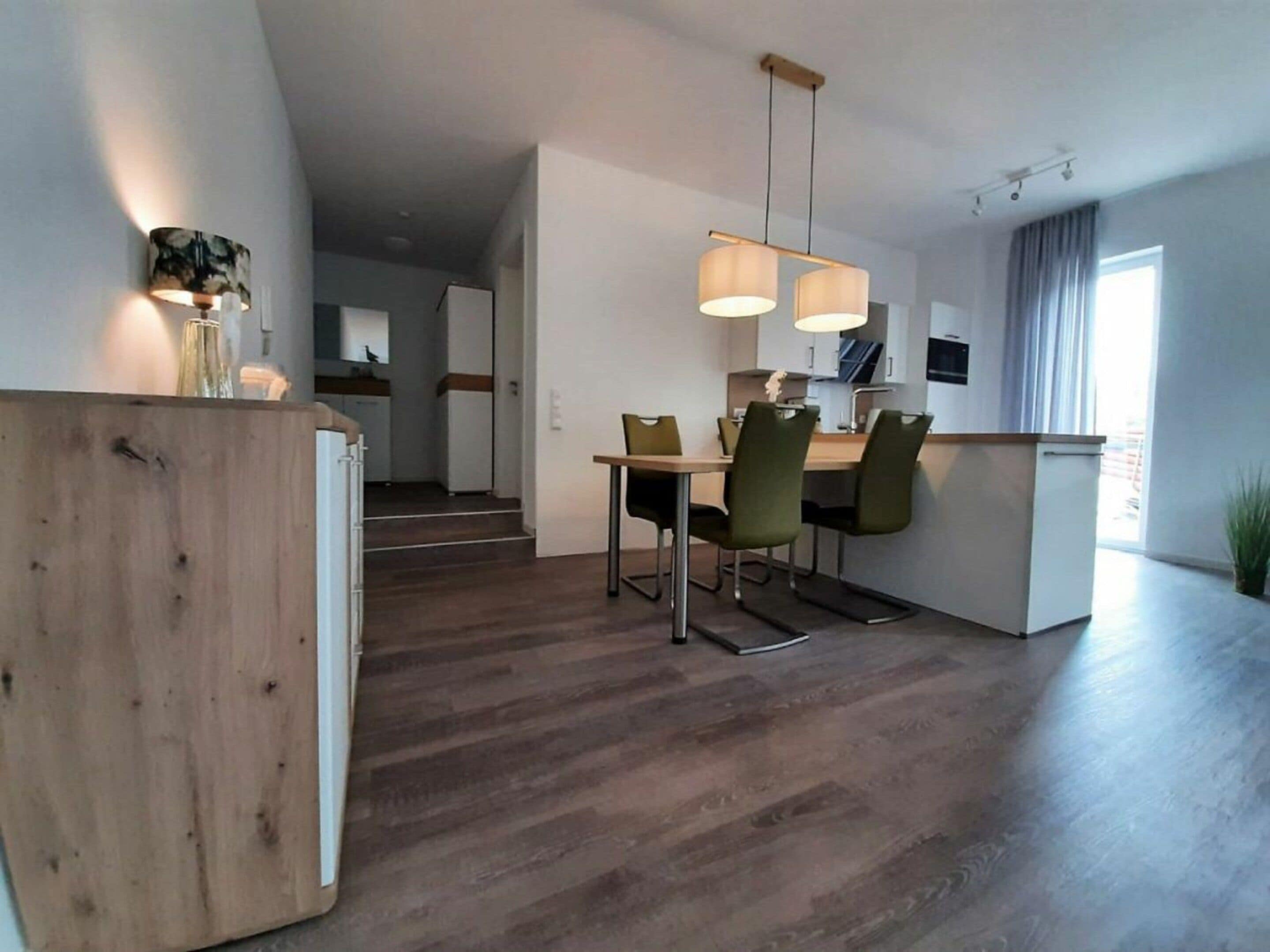 Cozinha moderna com área de jantar, piso de madeira e iluminação pendente.