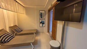 Um quarto com duas poltronas de vime, uma mesinha redonda e uma televisão de tela plana presa na parede.