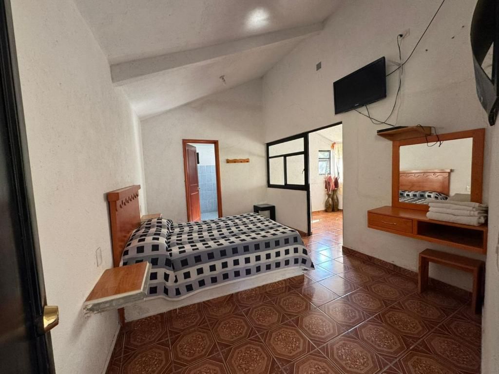 Quarto com cama, mesa de cabeceira, espelho e televisão na parede.