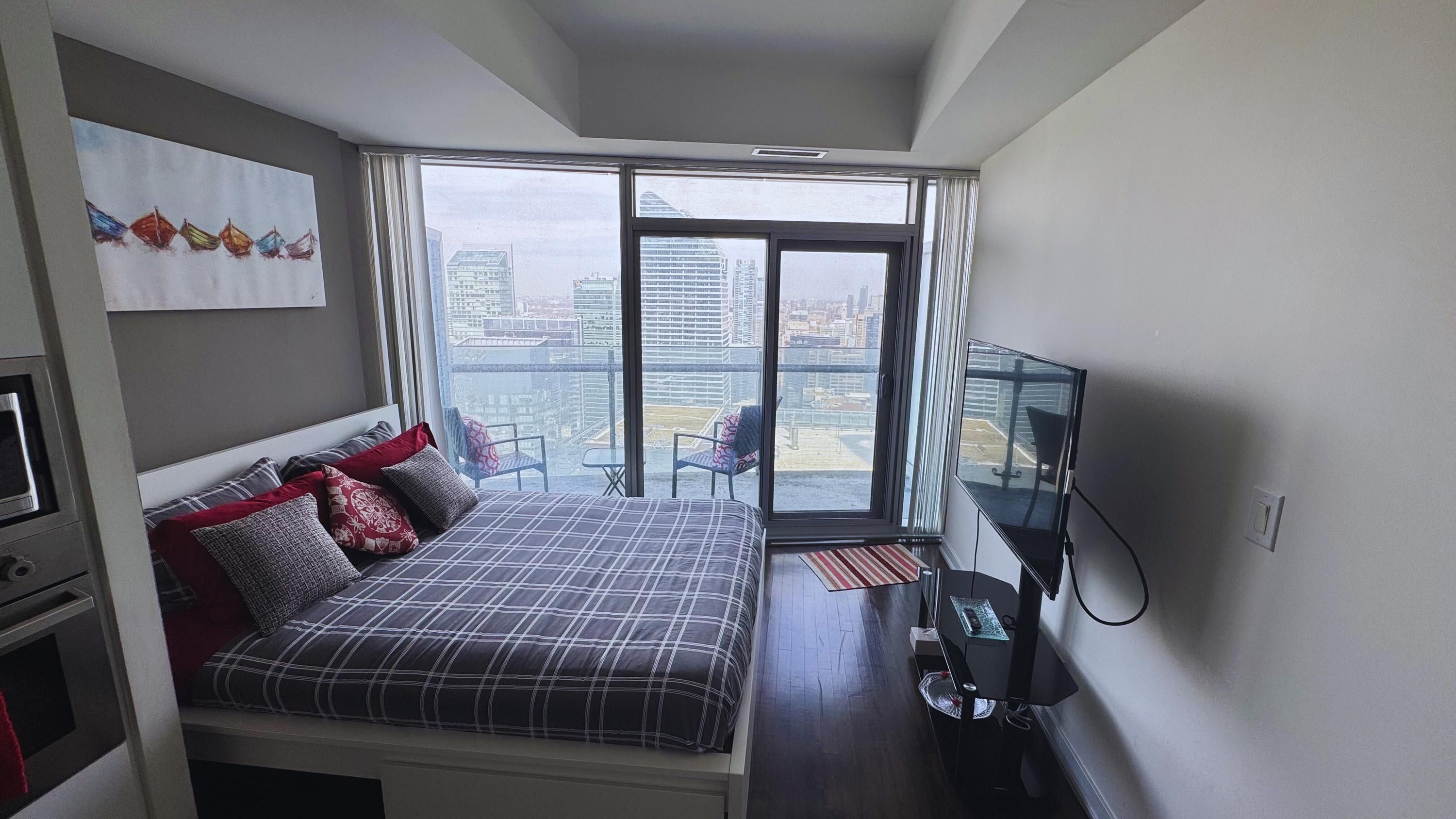Quarto moderno com uma cama grande, televisão e varanda com vista para a cidade.