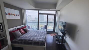 Quarto moderno com uma cama grande, televisão e varanda com vista para a cidade.