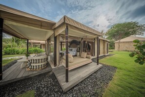 Uma área de estar coberta ao ar livre com sofá e balanço, cercada por um jardim e uma parede de pedra.