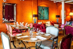 Uma sala de jantar com mesas redondas, cadeiras e uma parede de tijolos vermelhos.