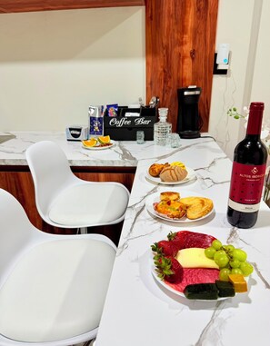 Uma mesa de jantar com um cantinho para café, uma garrafa de vinho e diversos alimentos.