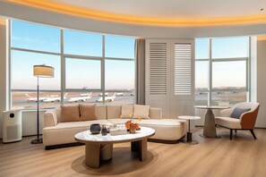 Quarto de hotel moderno com uma janela grande que oferece vista para um aeroporto.