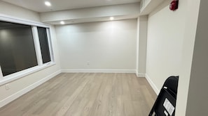 Quarto com uma grande janela, piso de madeira clara e paredes brancas.