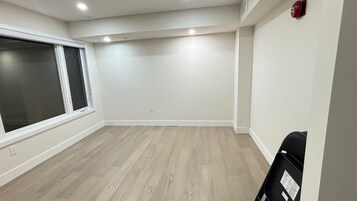 Quarto com uma grande janela, piso de madeira clara e paredes brancas.
