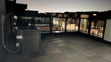Terraço no telhado com um aparelho de ar condicionado grande, uma divisória de vidro e vista para a paisagem urbana.
