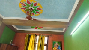 Quarto com ventoinha no teto, janela com cortinas e parede com um design colorido.