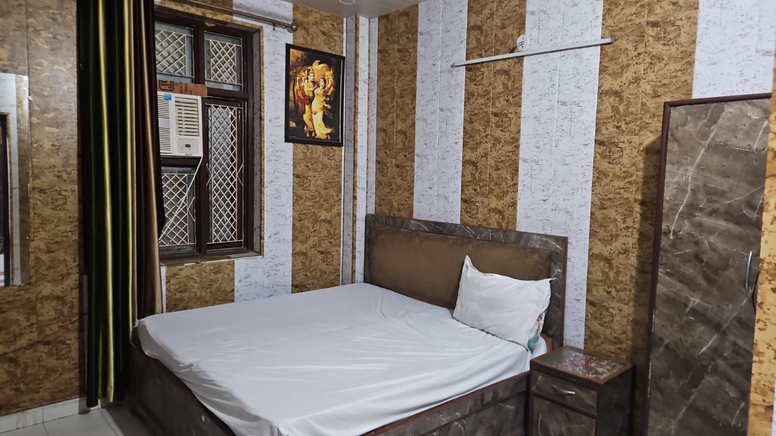 Quarto com cama, mesa de cabeceira, guarda-roupa, janela com grade de metal e quadro na parede.