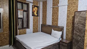 Quarto com cama, mesa de cabeceira, guarda-roupa, janela com grade de metal e quadro na parede.