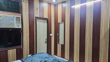 Quarto com paredes de madeira listrada, uma porta, um espelho pequeno e uma cama com cobertor azul.