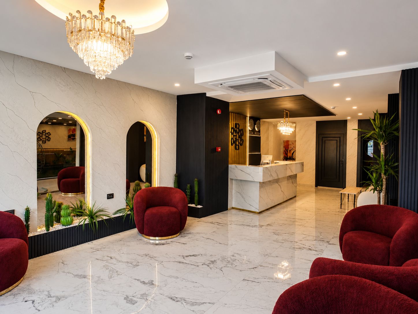 Um hall moderno com piso de mármore, cadeiras estofadas em vermelho, um balcão de recepção e um lustre.