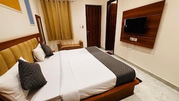 Quarto de hotel com cama, televisão fixada na parede e janela com cortinas.