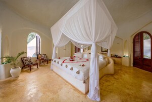 Quarto com cama de dossel, planta em vaso e vista pela janela arqueada.