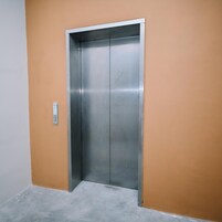 Porta de elevador metálica com painel de controle na parede ao lado.