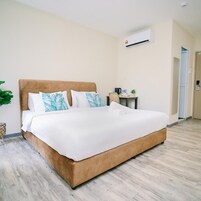 Quarto de hotel com uma cama grande, uma mesa de cabeceira, uma pequena planta e um ar condicionado.