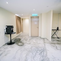 Corredor com uma porta fechada, uma mesa com um aparelho e uma placa indicando um banheiro.