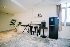 Cozinha compacta com geladeira, uma mesa pequena, dois banquinhos e um vaso com planta.