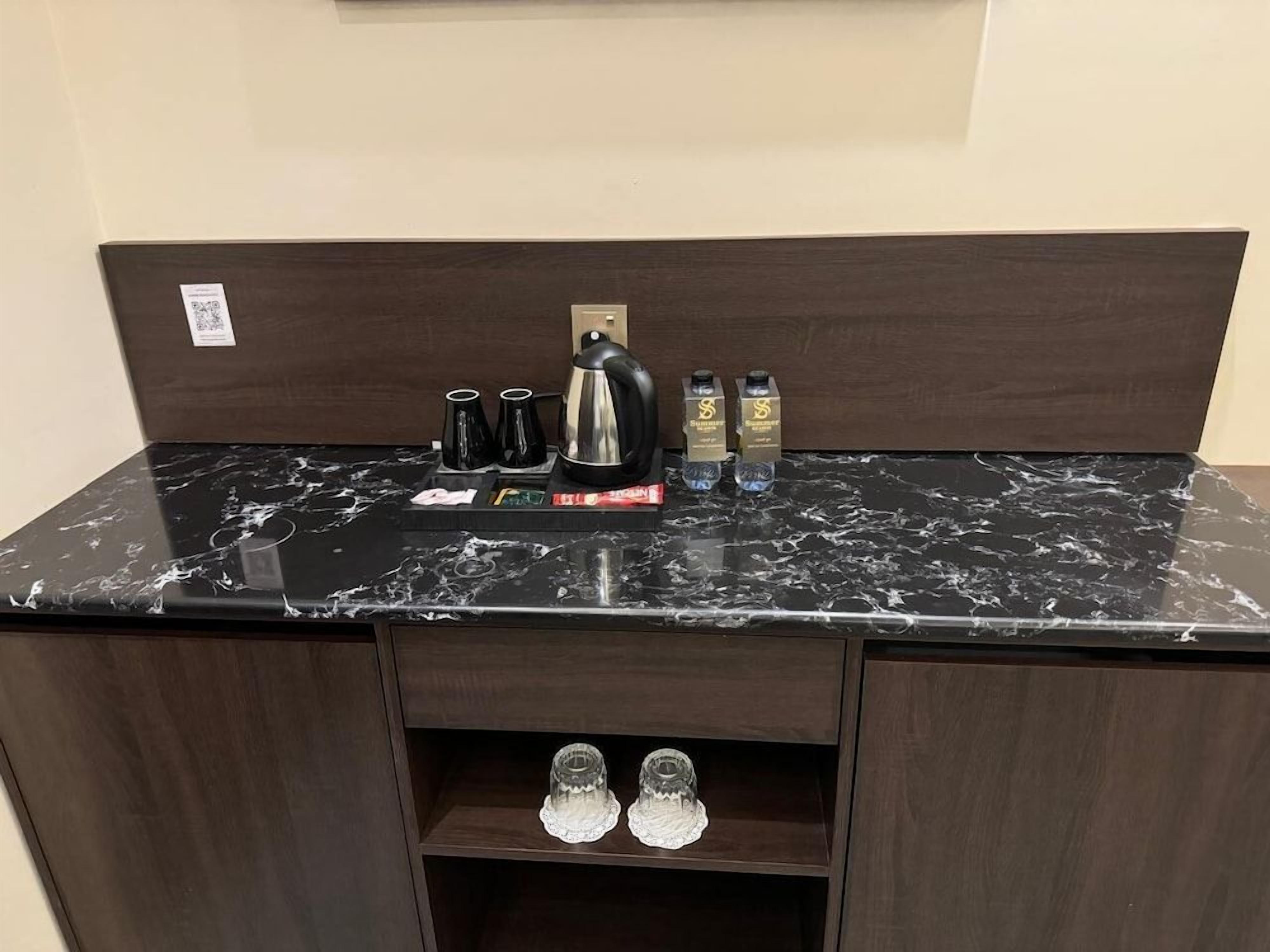 Uma bancada de mármore com uma cafeteira, chávenas e uma caixa de cápsulas de café.