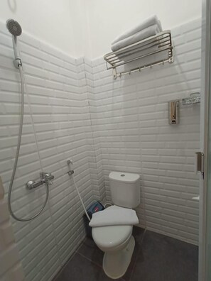 Um banheiro pequeno com azulejos brancos, chuveiro, vaso sanitário e porta-toalhas.