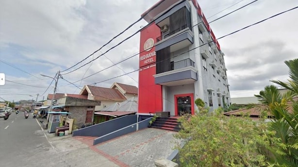 Um hotel com vários andares, fachada em vermelho e branco bem visível, entrada aparente e varanda no andar superior.