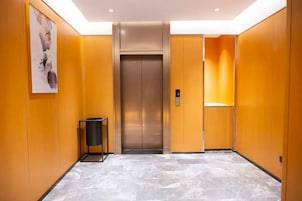 Elevador moderno em corredor com chão de mármore e lixeira na parede.